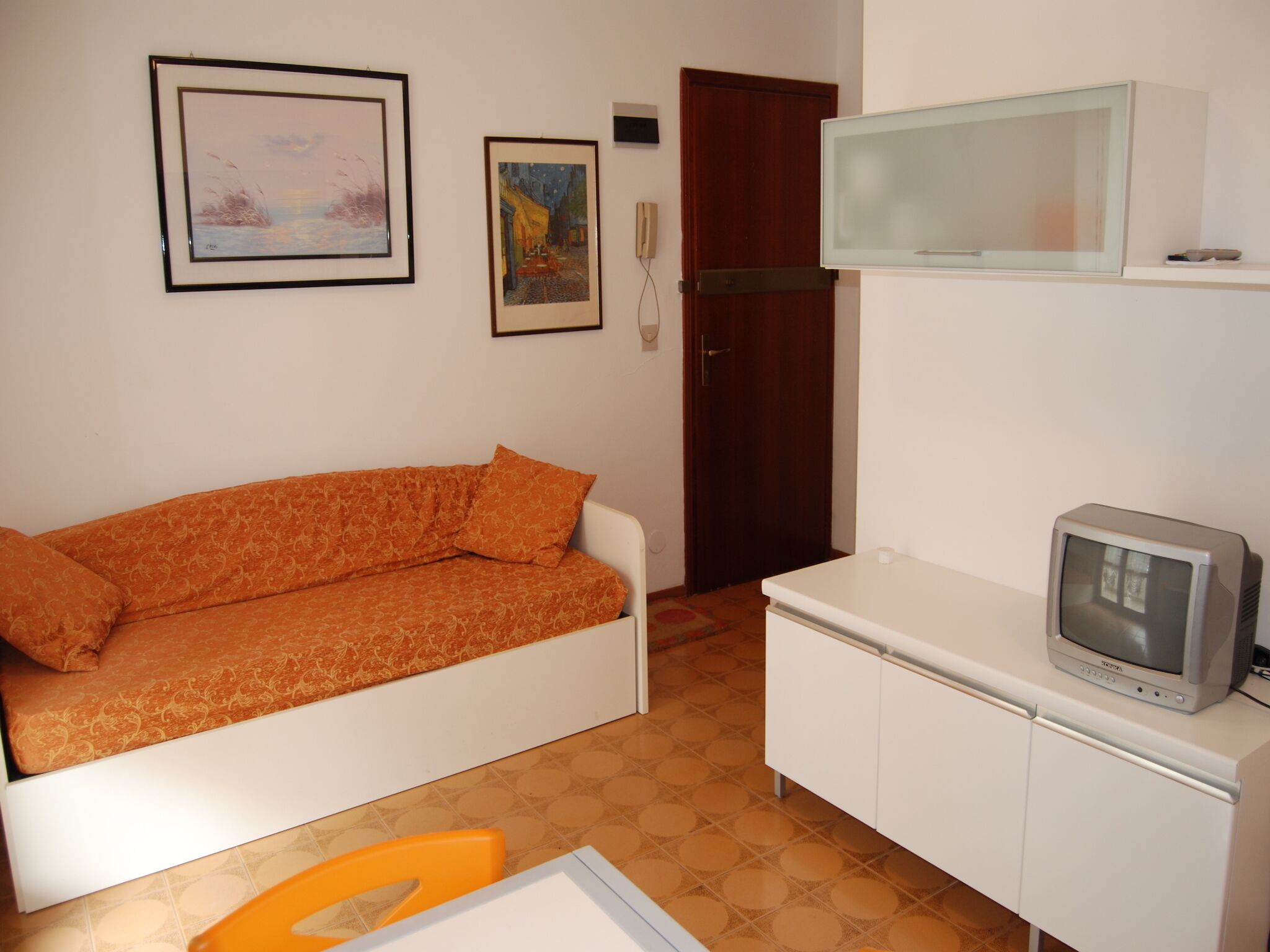 Quarto com sofá, televisão em um armário e duas molduras na parede.