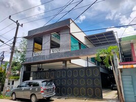 Um edifício moderno de dois andares com entrada de garagem, um carro estacionado em frente e uma palmeira por perto.