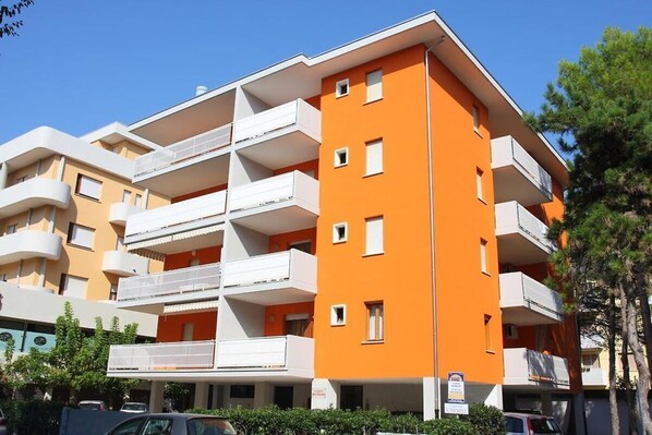 Um edifício com várias andares, varandas, estacionamento e áreas verdes.