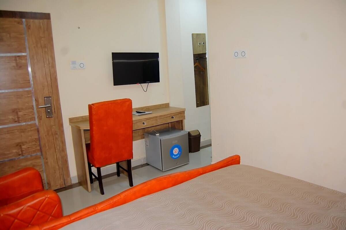 Quarto com cama, escrivaninha, cadeira, televisão e um pequeno cofre.