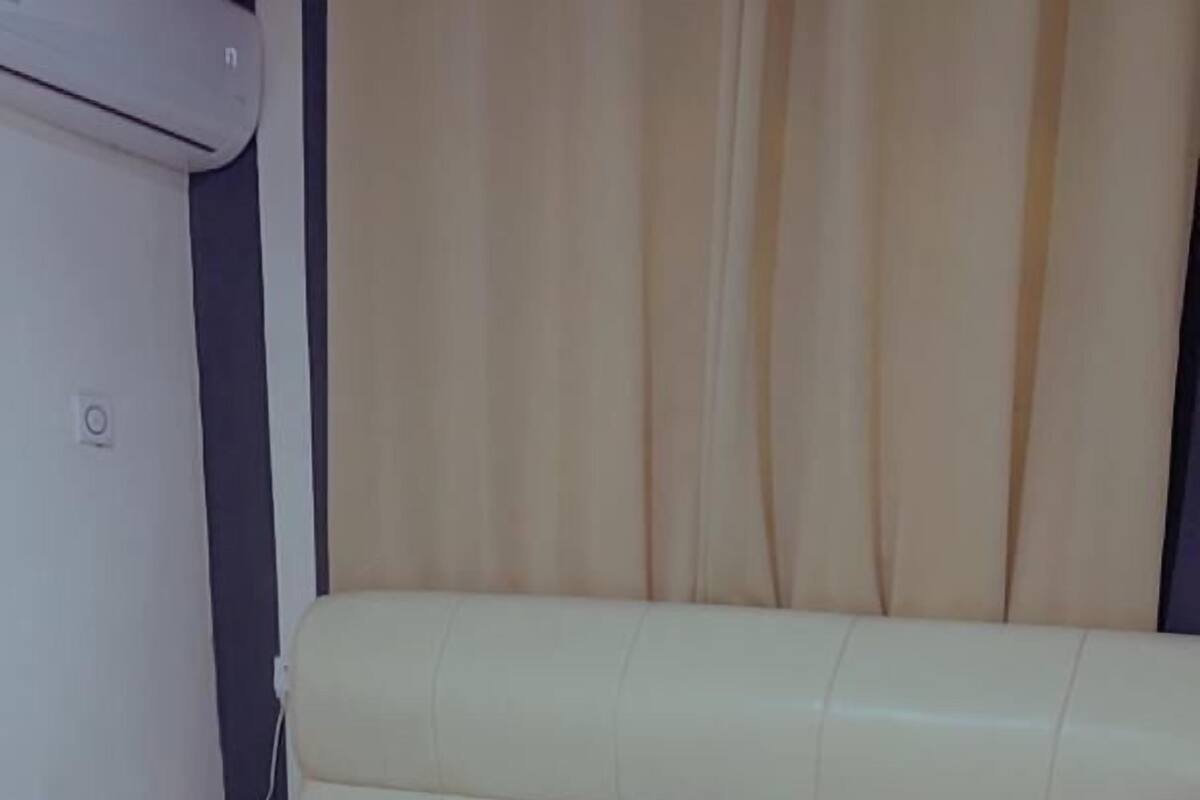 Cama com colchão e almofadas brancas, mesa de cabeceira com abajur e ar-condicionado fixado na parede.