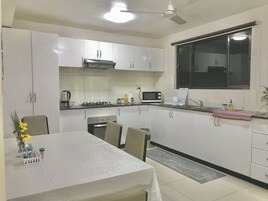 Cozinha moderna com armários brancos, fogão a gás, micro-ondas e área de jantar com mesa e cadeiras.
