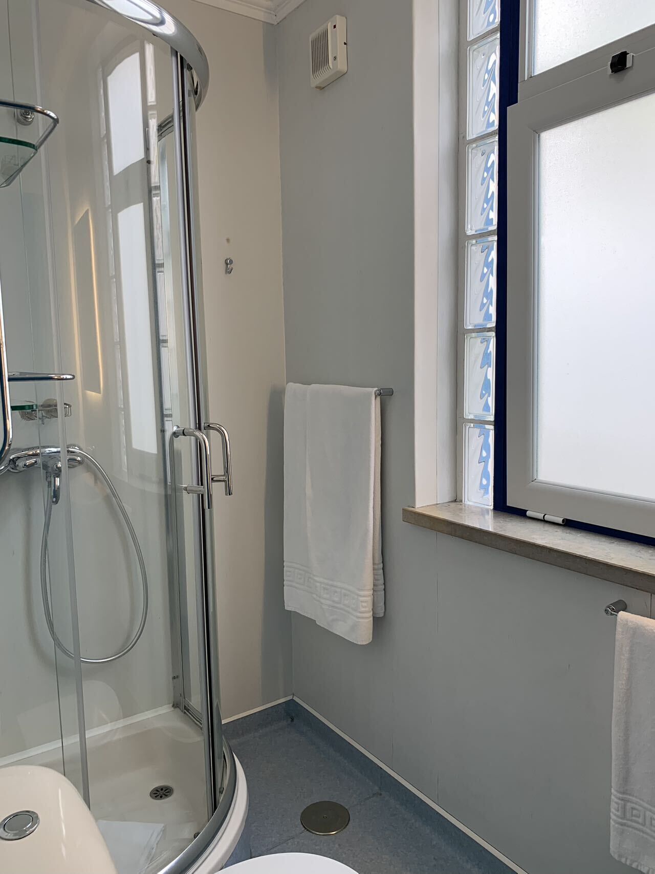 Casa de banho moderna com cabine de chuveiro em vidro, lavatório branco e janela com persianas estampadas.
