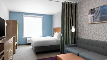 Quarto de hotel com cama, sofá, escrivaninha e televisão.