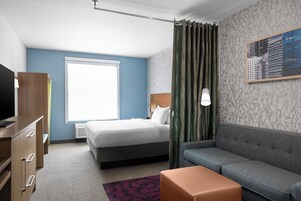 Quarto de hotel com cama, sofá, escrivaninha e televisão.