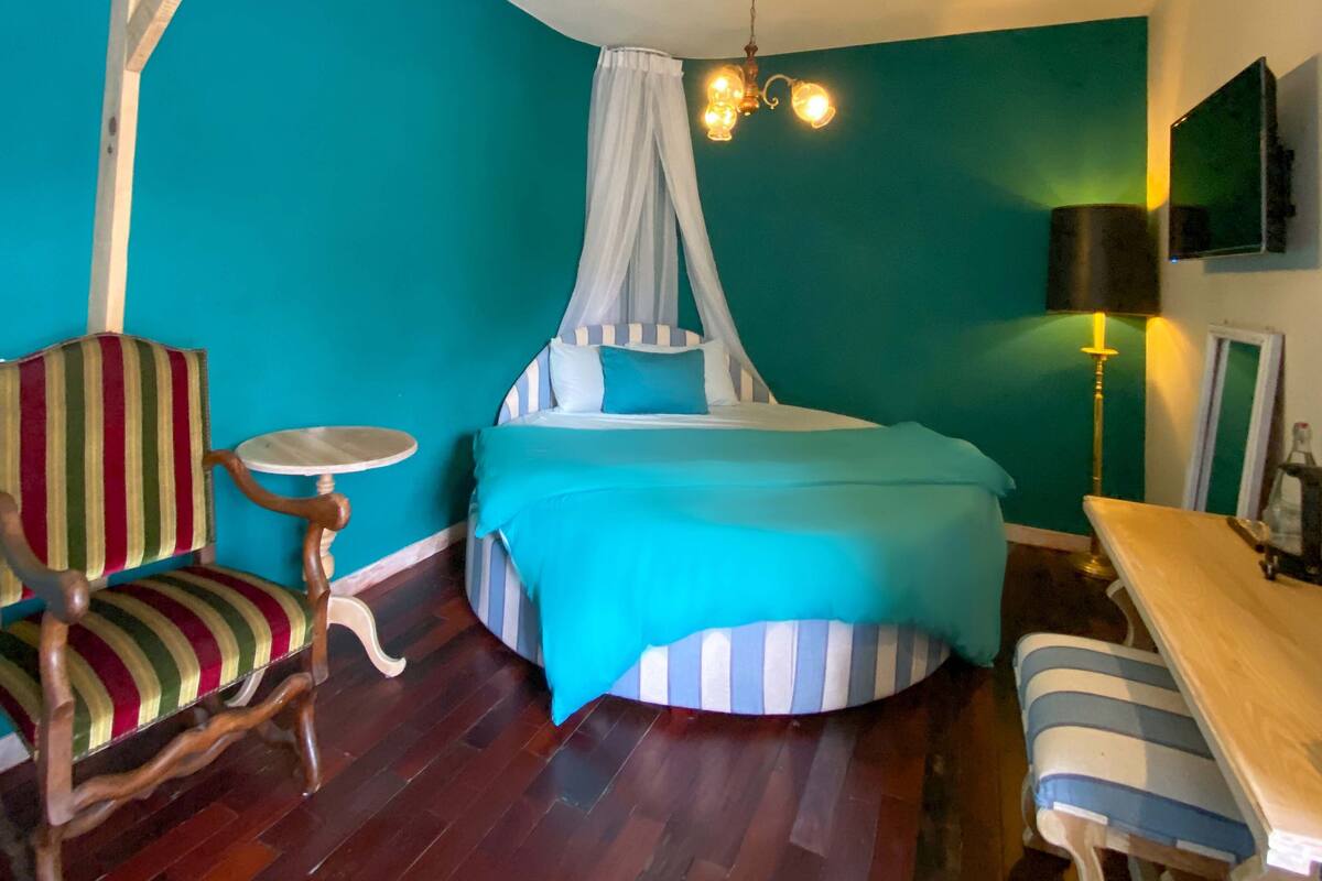 Quarto com cama, cadeira, mesa pequena, banquinho e luminária.