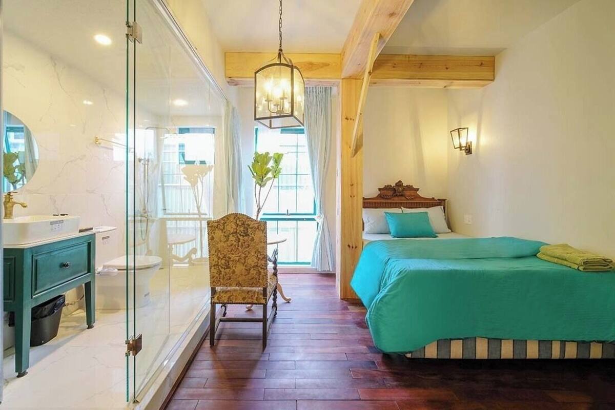 Quarto com cama, cadeira, mesa de cabeceira, espelho e janela.