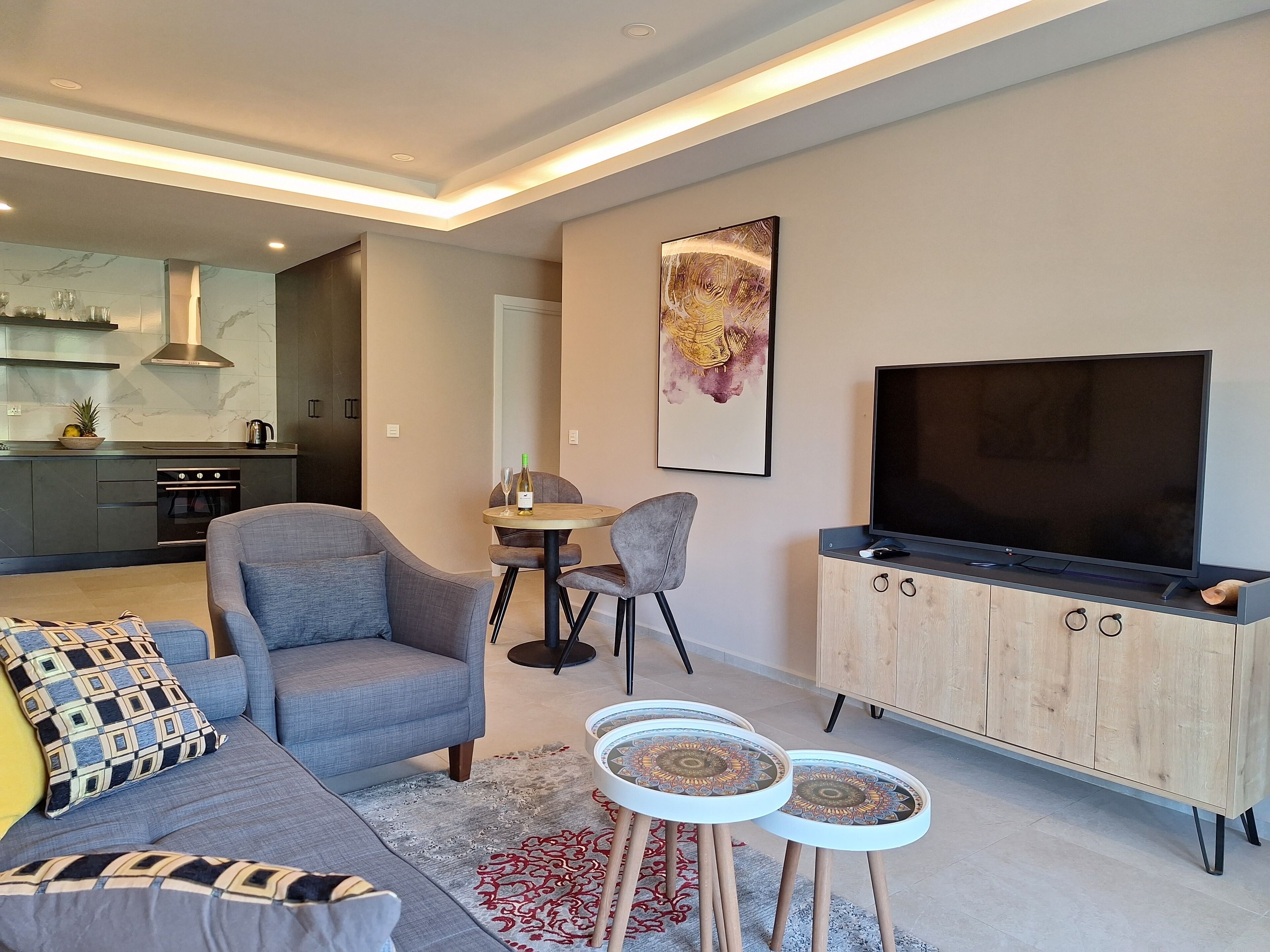 Uma sala de estar moderna com um sofá cinzento, uma televisão e uma área de jantar com mesa e cadeiras.