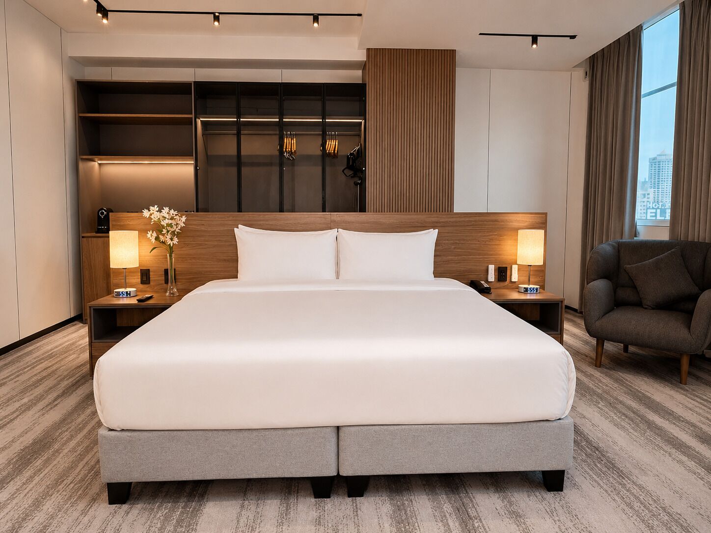Quarto de hotel moderno com uma cama grande, mesas de cabeceira, um criado-mudo, uma poltrona e vista para a cidade.