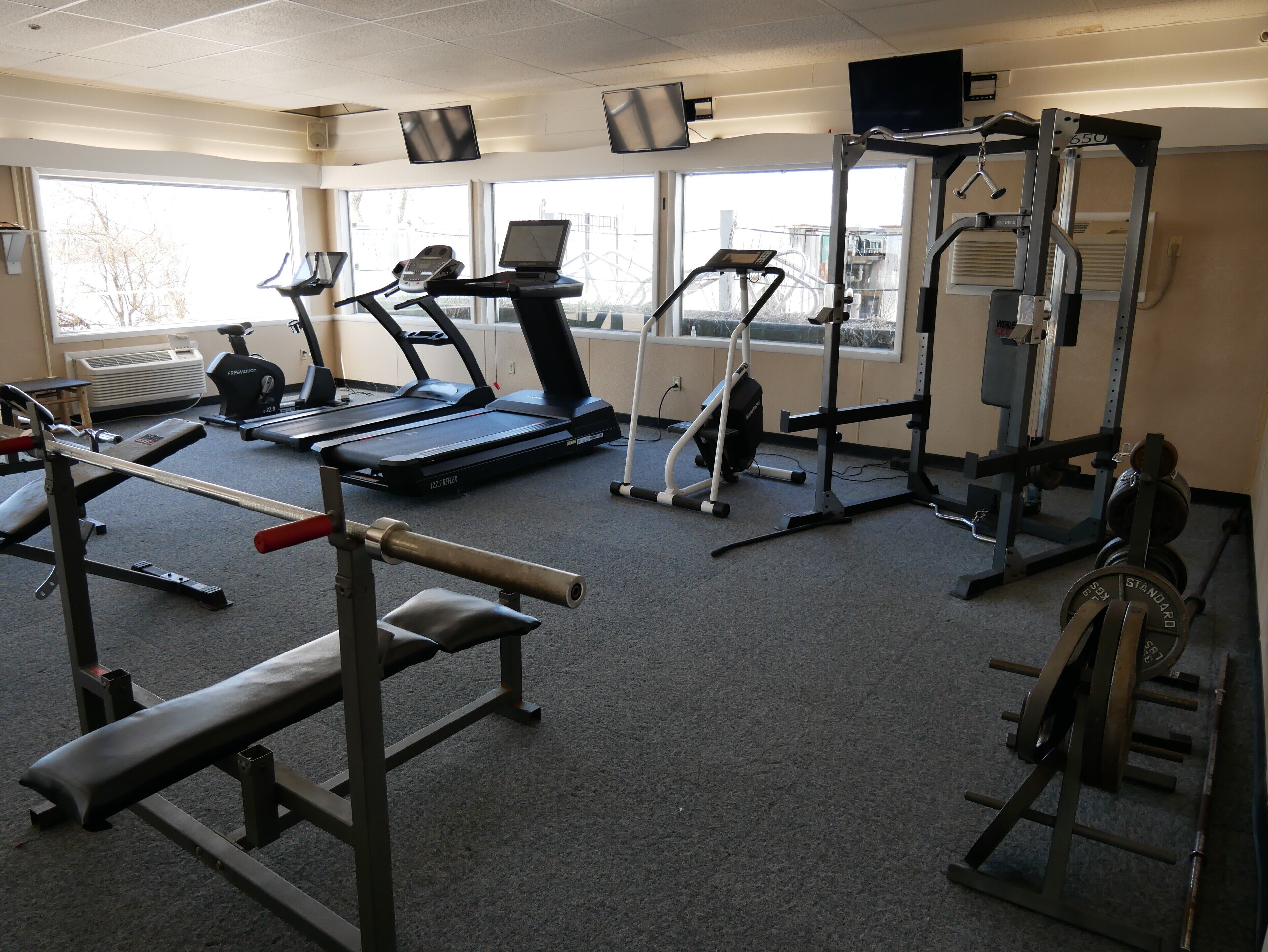 Uma academia com esteiras, aparelhos de musculação e um banco.