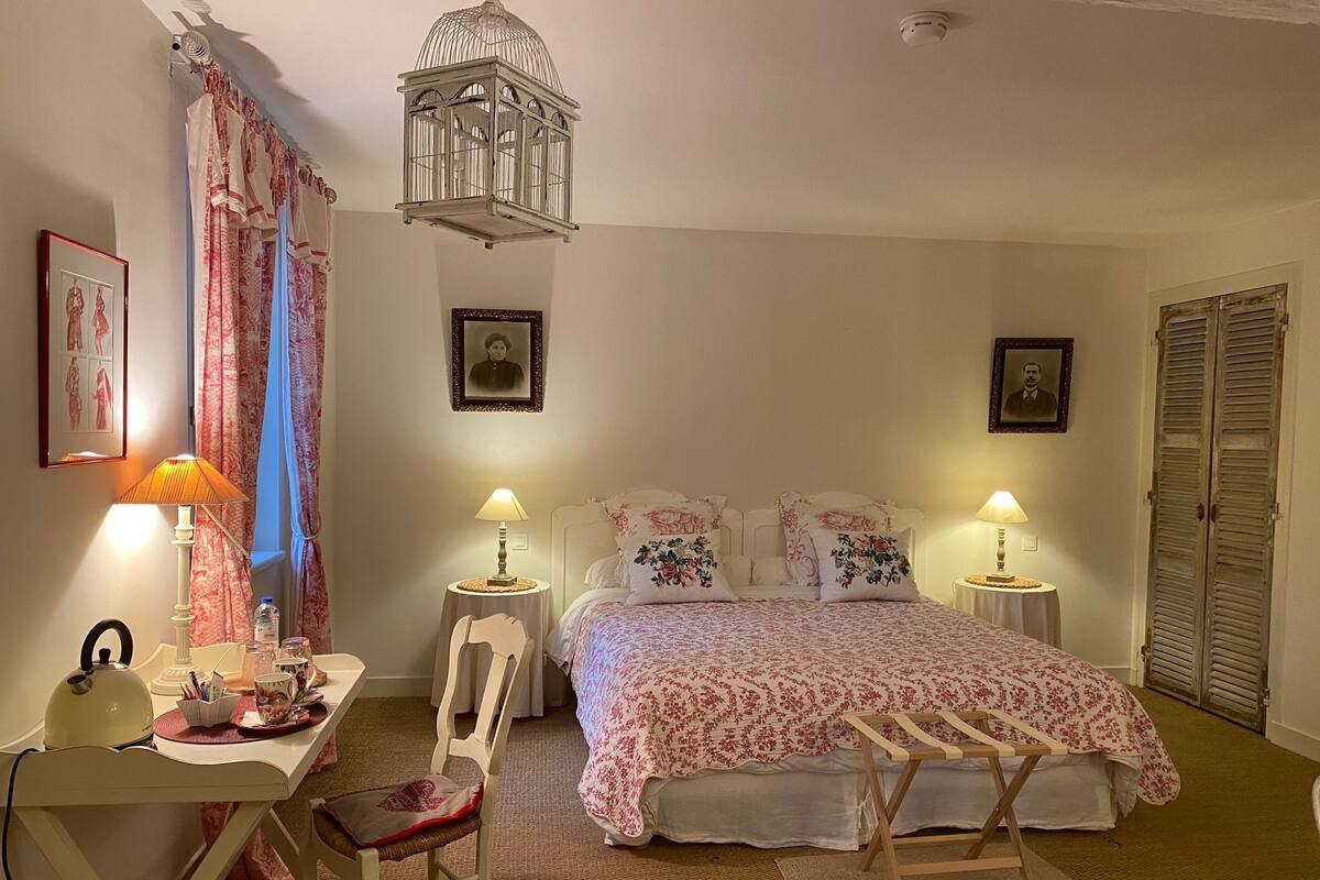 Um quarto aconchegante com uma cama, duas mesas de cabeceira com abajures, uma escrivaninha com cadeira, um radiador e um guarda-roupa.