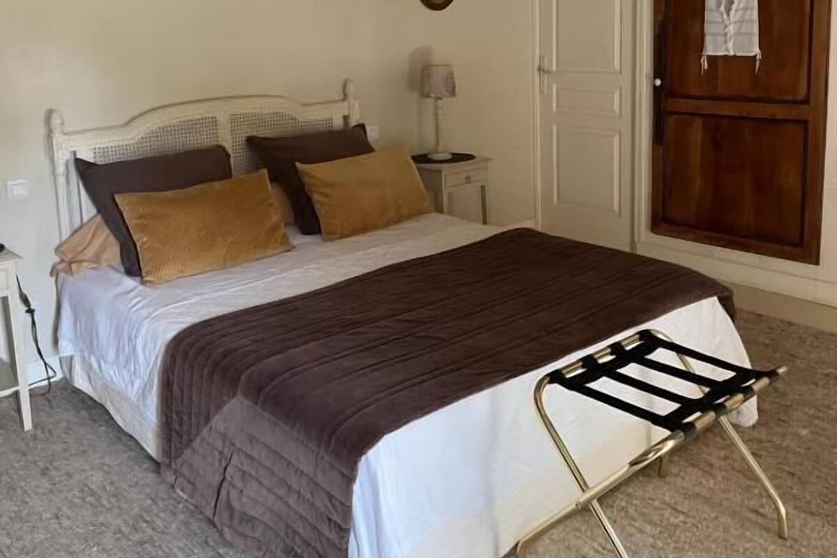Um quarto com cama, mesa de cabeceira, porta de madeira e um cabideiro.