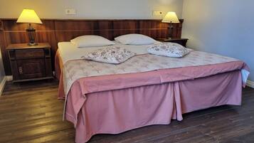 Uma cama de casal com saia rosa, duas luminárias de cabeceira e um painel de cabeceira de madeira.