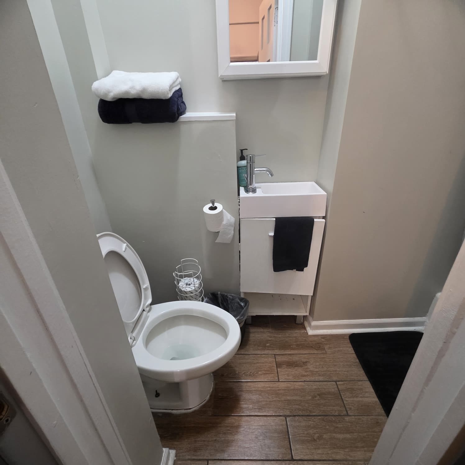 Casa de banho compacta com sanita, lavatório e pequena prateleira sobre o lavatório.