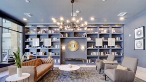 Uma sala de estar moderna com um sofá, poltronas, uma mesa de centro e uma estante repleta de livros e objetos decorativos.
