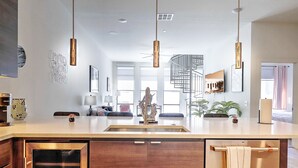 Uma cozinha moderna com uma ilha central, luminárias pendentes e uma escada em espiral ao fundo.