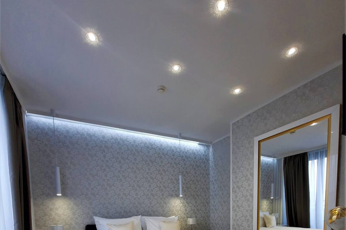 Quarto moderno com cama grande, mesas de cabeceira, espelho e iluminação embutida no teto.