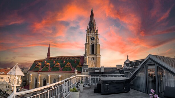 Terraço no telhado com vista para o campanário de uma igreja, varanda com guarda-corpo e um pequeno jardim.