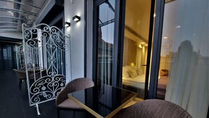 Quarto de hotel moderno com porta de vidro que dá para um quarto, área de jantar com mesa e cadeiras, e divisória metálica decorativa.
