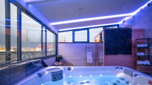 Um spa moderno com banheira de hidromassagem, janelas amplas e parede de madeira com planta suspensa verde.