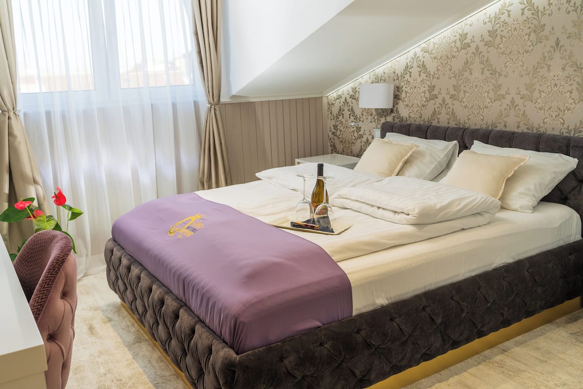 Quarto com uma cama grande, mesa de cabeceira, abajur e janela com cortinas.