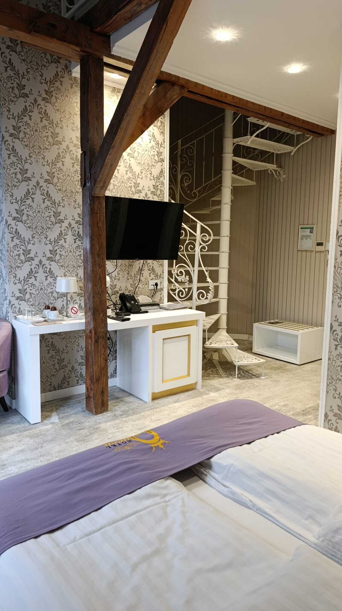 Quarto com uma cama, uma escrivaninha com computador, uma televisão e uma escada.
