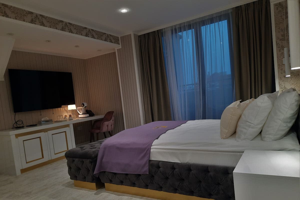 Quarto de hotel moderno com uma cama grande, uma escrivaninha com computador e uma televisão de tela plana.