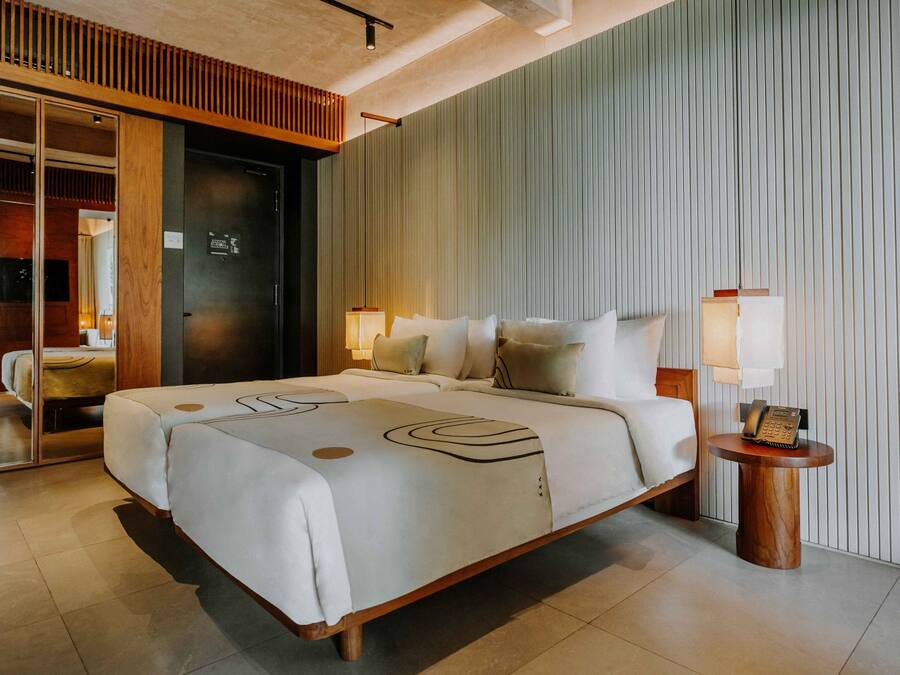 Quarto de hotel moderno com uma cama grande, abajures, mesa de cabeceira de madeira e um espelho.