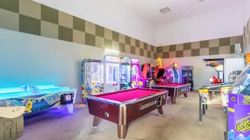 Um espaço com mesas de bilhar, jogos de fliperama e um padrão de parede quadriculado.