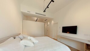 Quarto moderno com uma cama grande, televisão na parede e closet espaçoso.