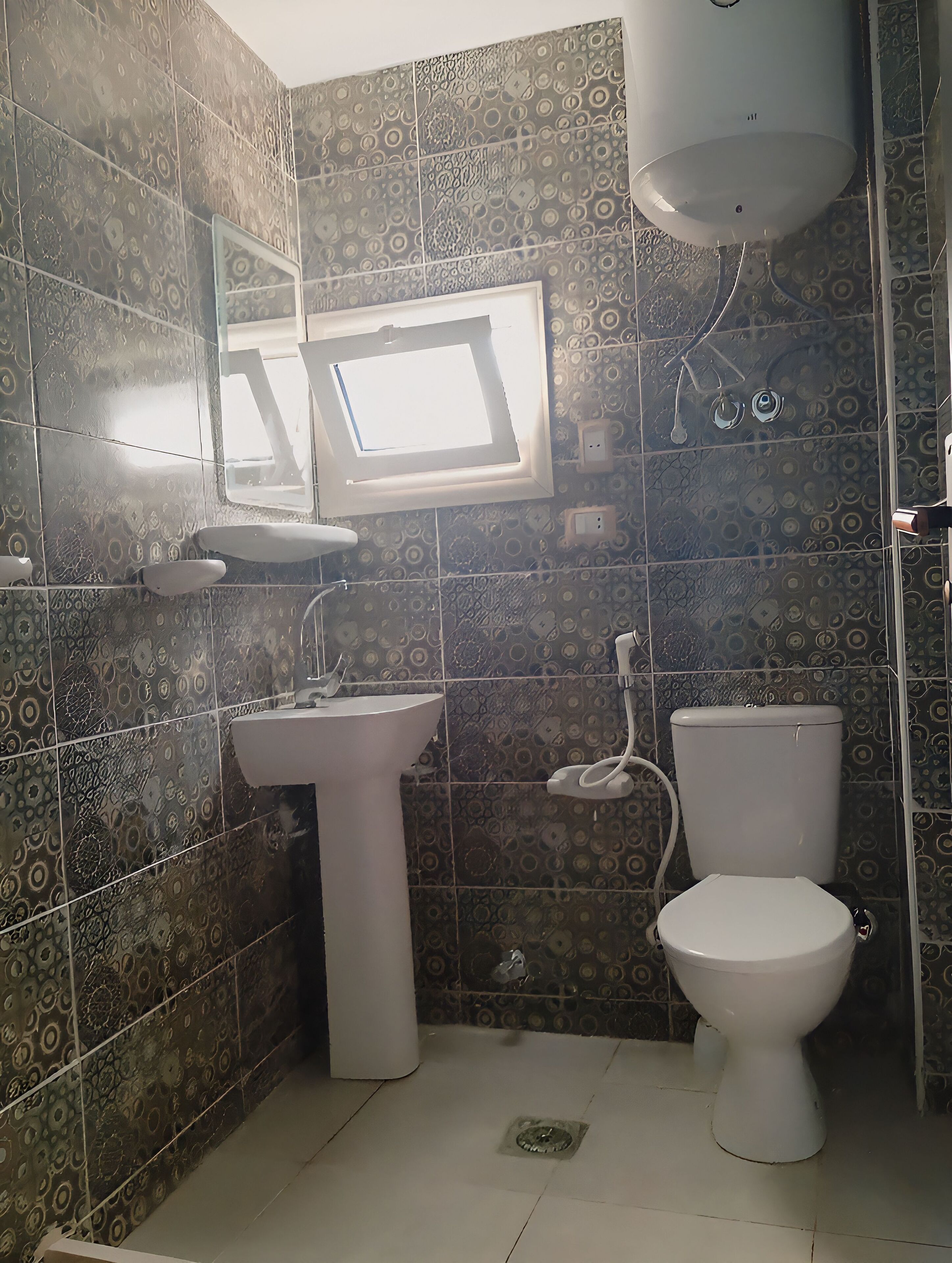 Um banheiro com azulejos estampados, pia de pedestal, vaso sanitário e janela sobre a pia.