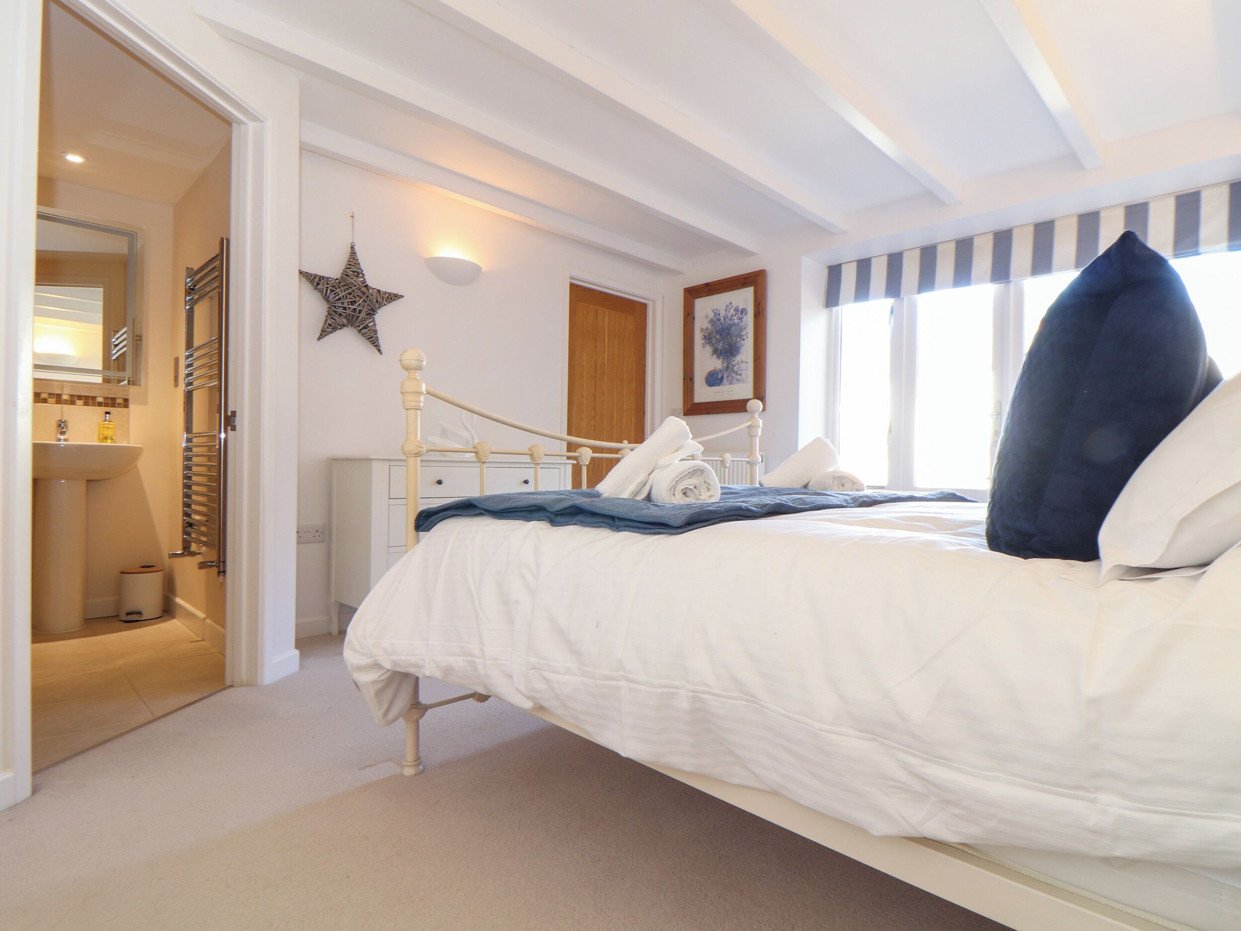 Quarto com cama, mesa de cabeceira, luminária de parede, decoração em formato de estrela, quadro e janela com cortinas.