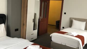 Quarto de hotel com duas camas, um guarda-roupa e uma porta que dá para outro espaço.
