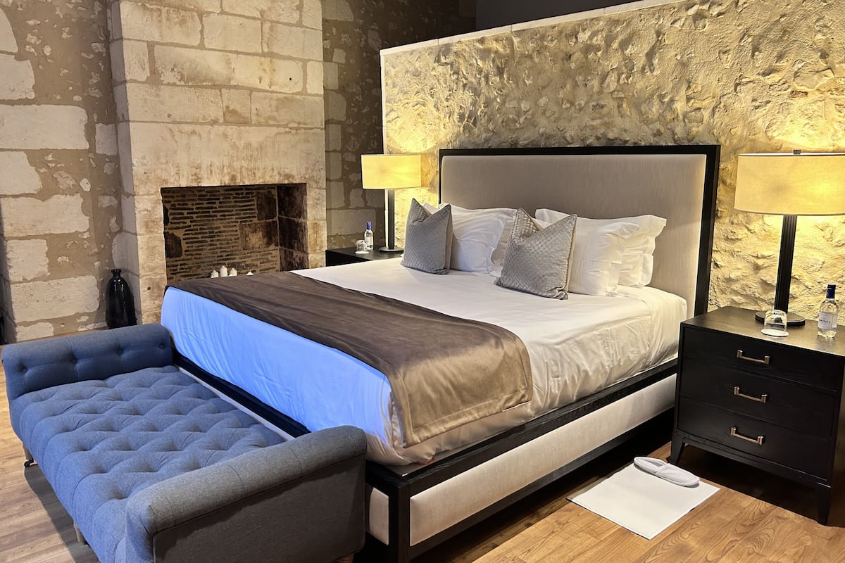 Um quarto com uma cama grande, lareira, mesa de cabeceira e uma cadeira.