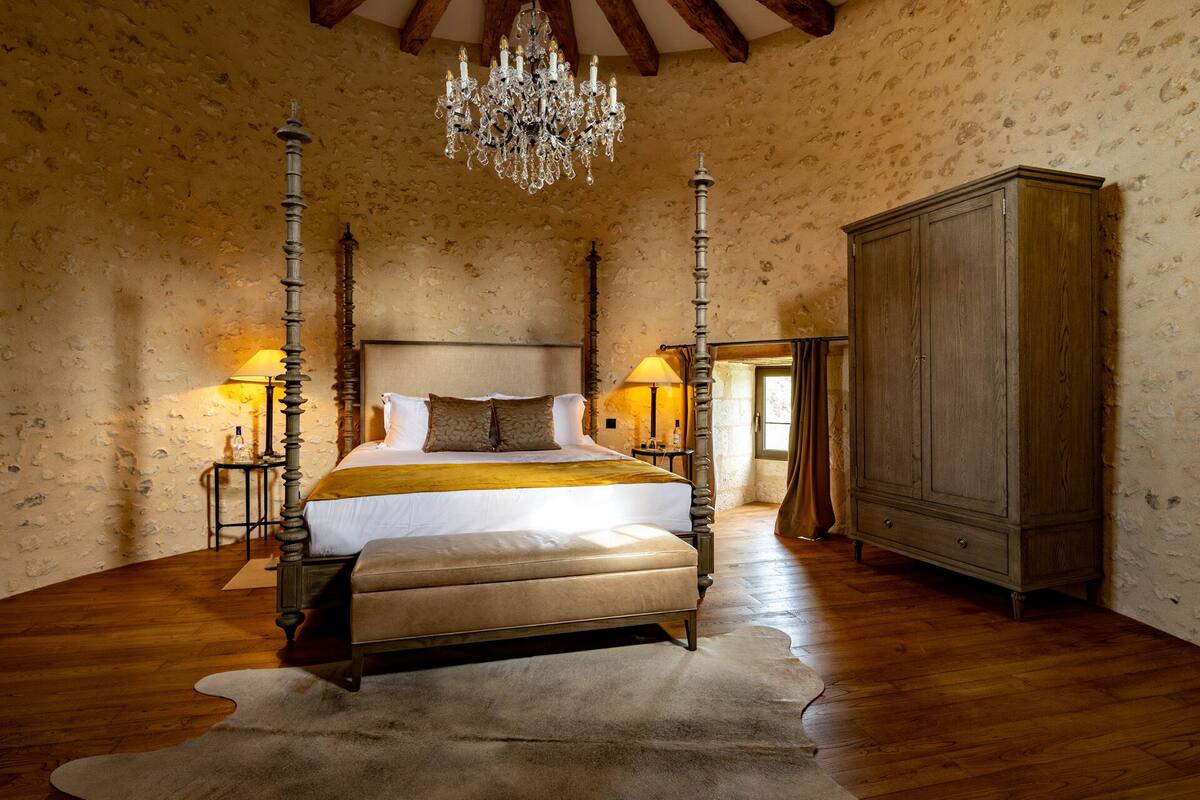 Quarto com cama de dossel, lustre, piso de madeira e guarda-roupa grande.