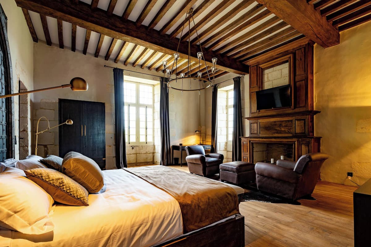 Quarto com vigas de madeira aparentes, uma cama grande, televisão e lareira.
