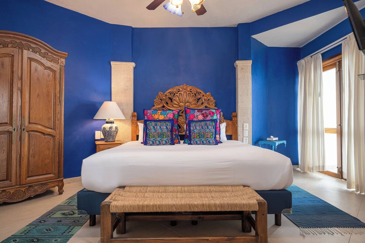 Quarto com uma cama grande, um guarda-roupa de madeira, uma mesa de cabeceira com abajur e uma janela com cortinas.