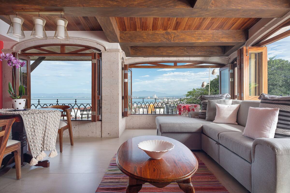 Uma sala de estar aconchegante com sofá, mesa de centro de madeira e varanda com vista.