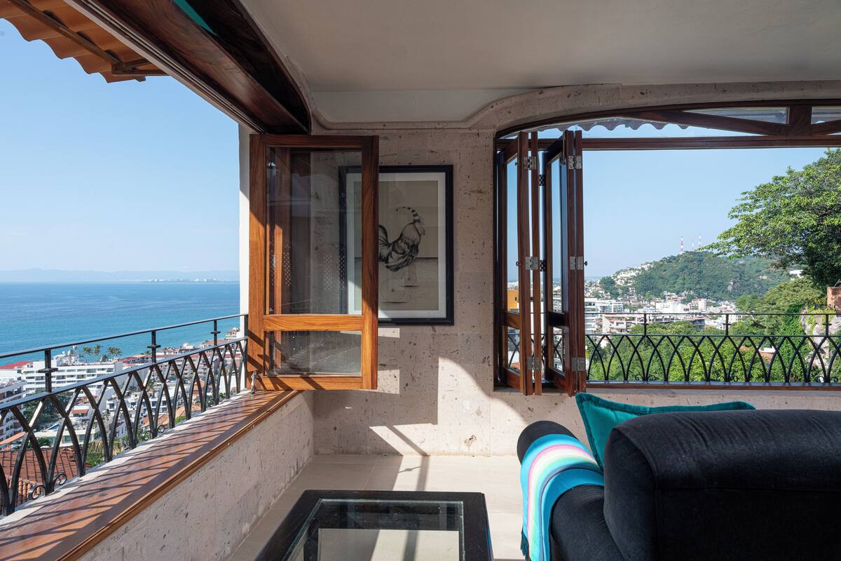 Uma varanda com vista para o mar, um quadro emoldurado e um sofá com almofadas.