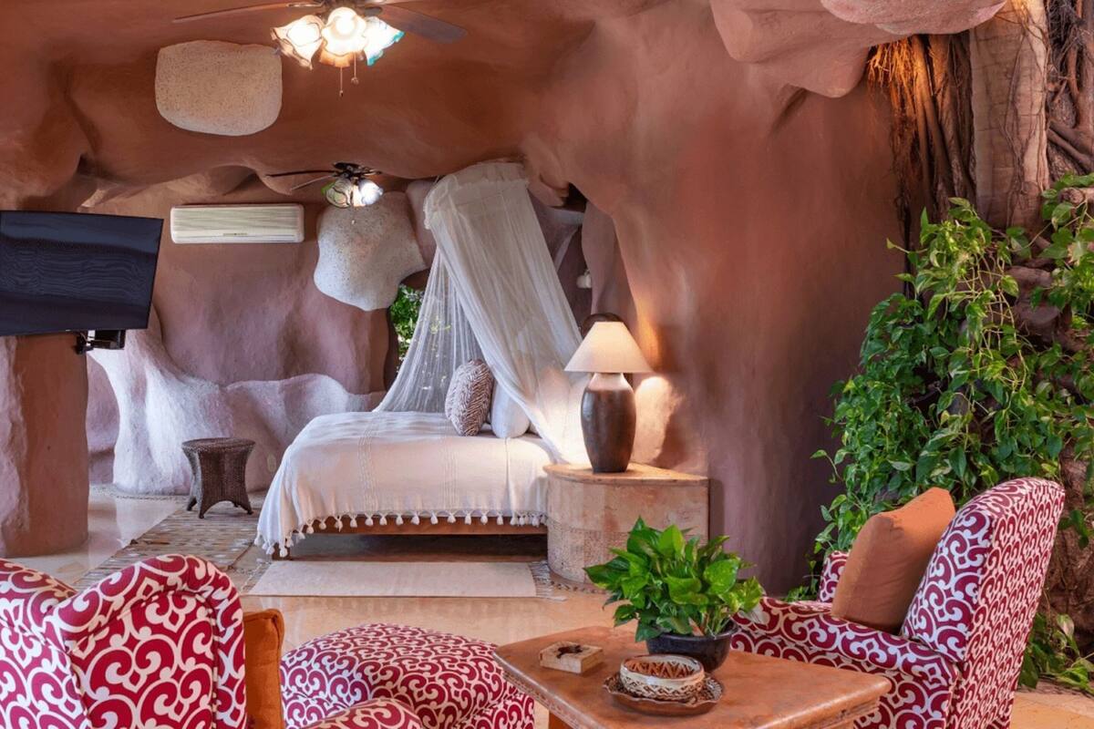 Quarto com cama, televisão, luminária e uma pequena mesa com uma planta.