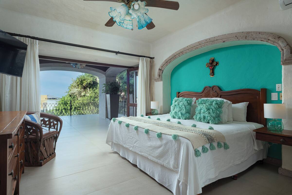 Quarto com cama, cômoda de madeira, cadeira e varanda com vista.