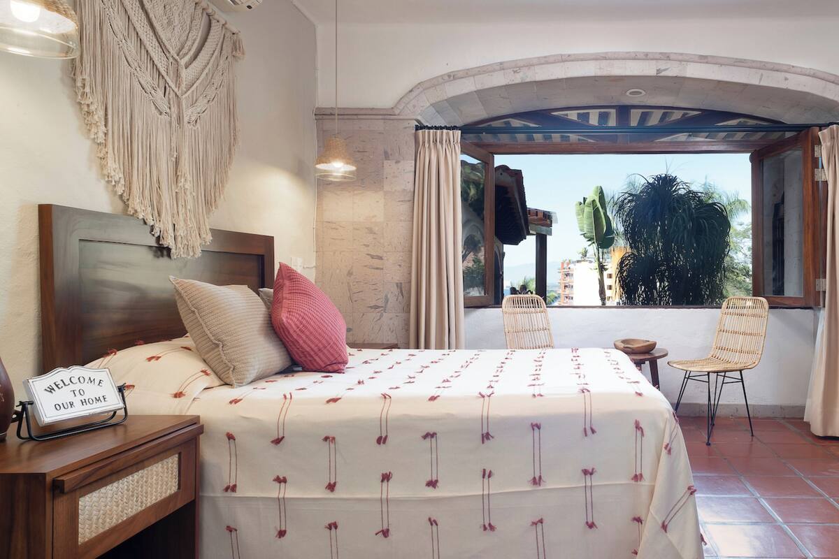 Quarto com cama, placa de boas-vindas, cadeira de vime, mesa de madeira e televisão.
