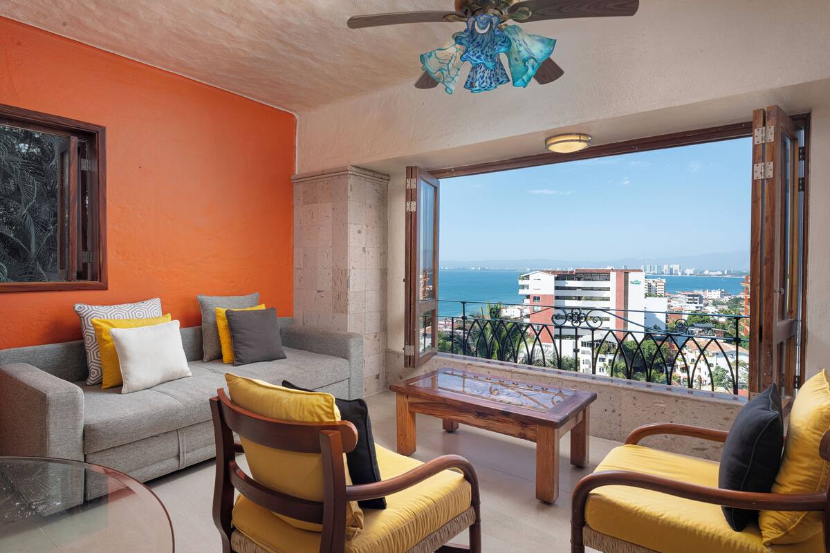 Sala de estar com sofá, poltronas, mesinha de centro e varanda com vista para a cidade e o mar.