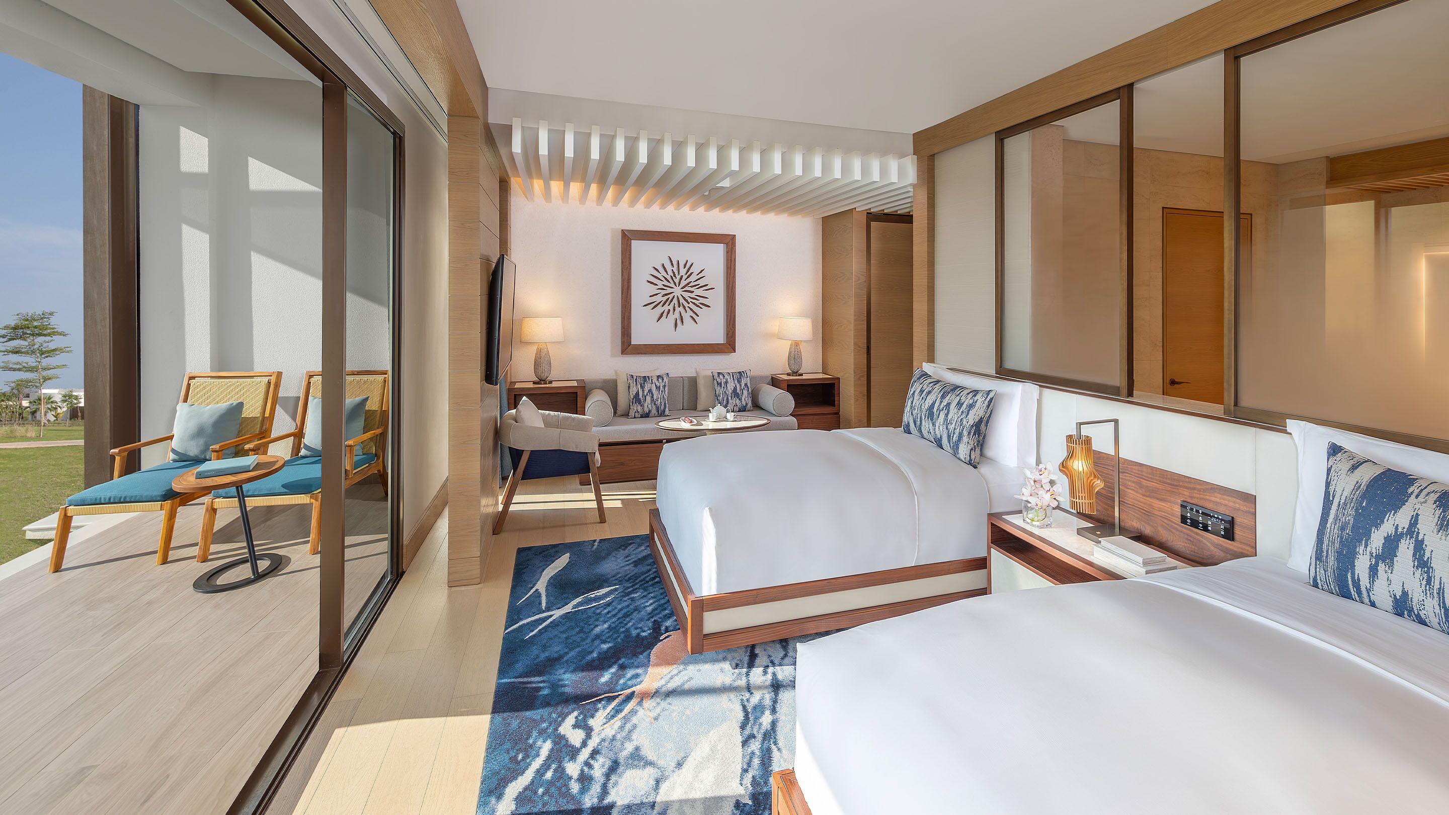 Quarto de hotel moderno com uma cama grande, um sofá, uma cadeira e uma escrivaninha. Há uma janela ampla e vista para o exterior.