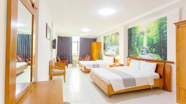 Quarto de hotel com duas camas, uma escrivaninha, cadeiras, um espelho grande e um quadro de uma trilha na floresta.