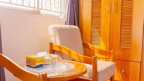 Quarto com cadeira e mesa de madeira, guarda-roupa de madeira e janela com persianas.