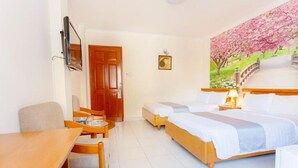Quarto de hotel com cama de madeira, uma mesinha com cadeiras, televisão na parede e um quadro de flores de cerejeira.