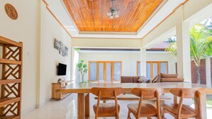 Uma sala de estar ampla com teto de madeira, uma mesa de jantar com cadeiras, um sofá e uma televisão na parede.