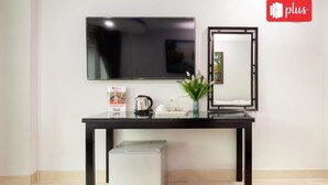 Quarto de hotel moderno com televisão de tela plana na parede, uma mesinha com chaleira e um vaso de flores, e um refrigerador compacto.