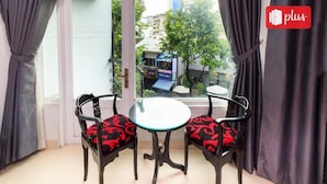 Varanda com duas cadeiras, uma mesa pequena, cortinas e vista para edifícios e árvores.